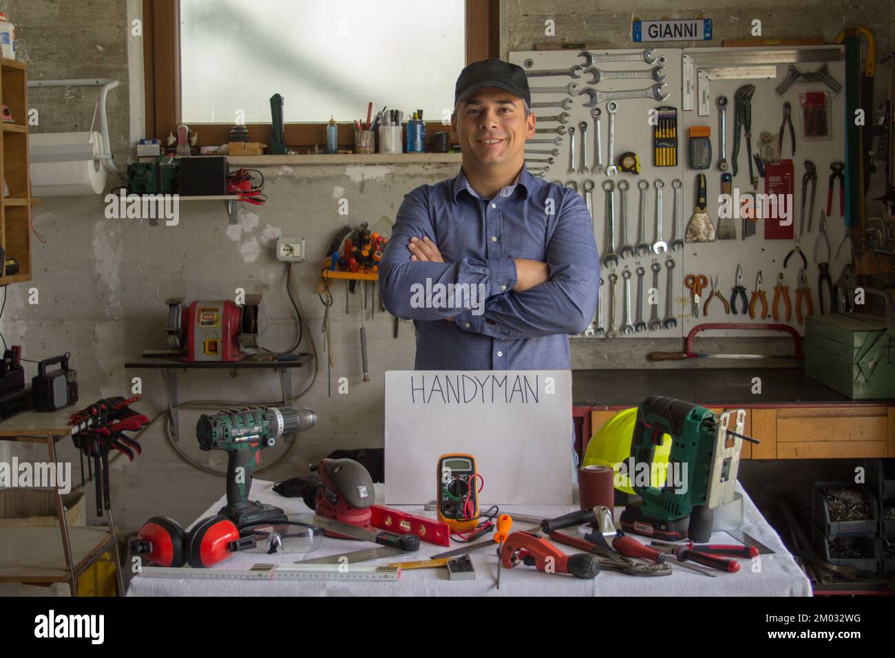 Image of a smiling man in his workshop with a bench full of work tools ...
