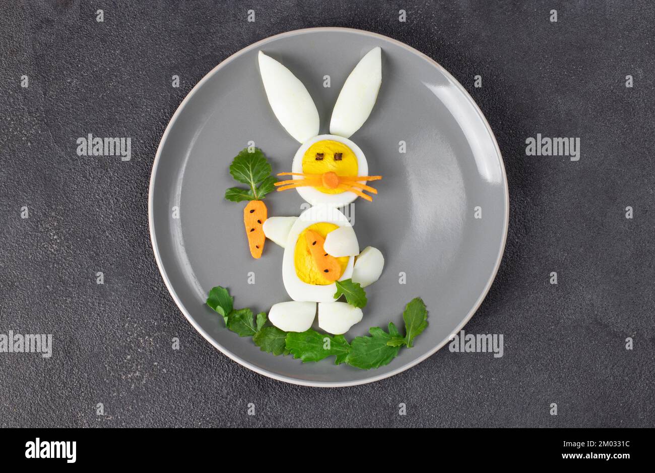Funny rabbit made from boiled eggs, peeled carrots and arugula on gray ...