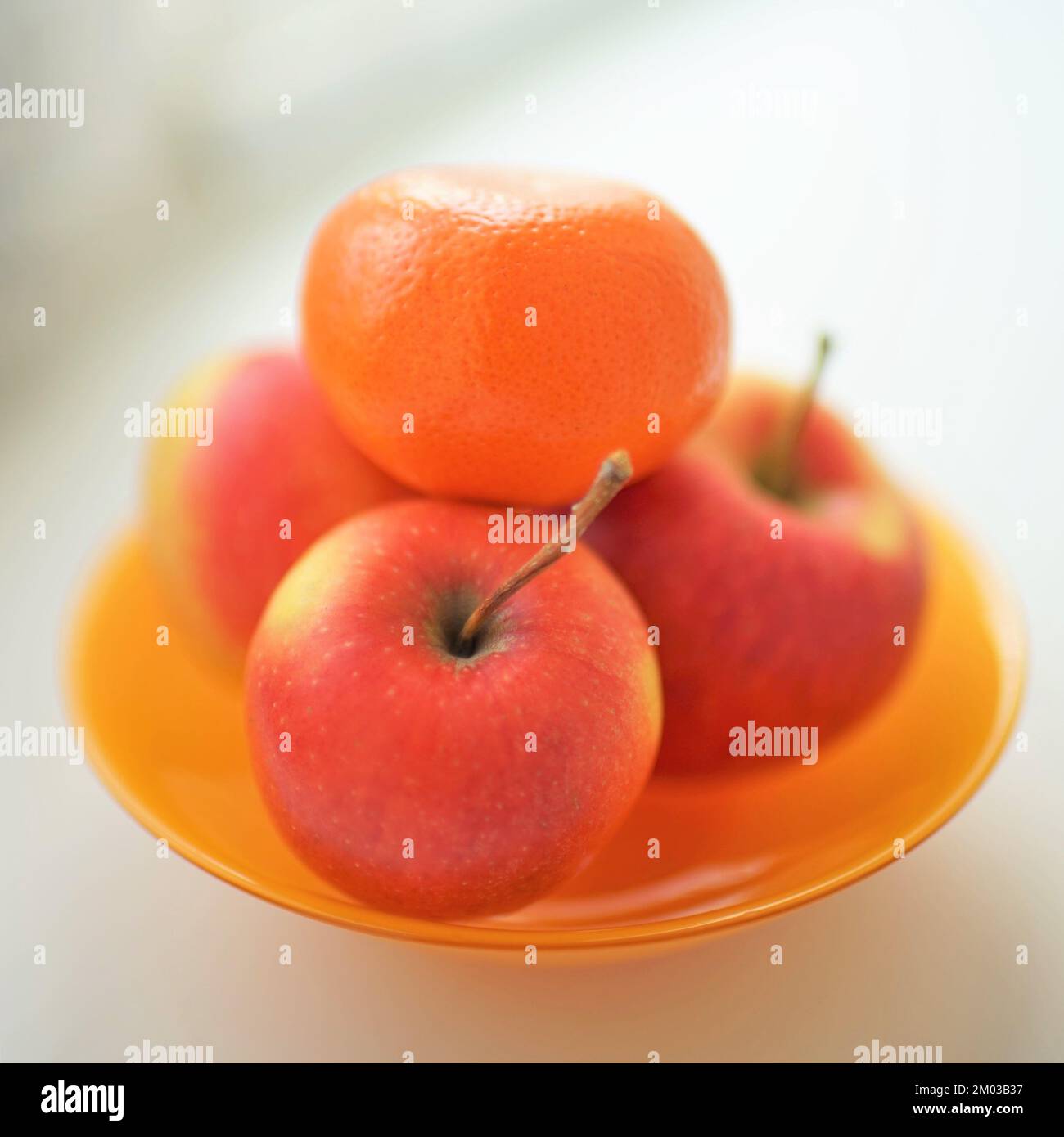 tangerine and three red apples in orange plate on the wite table Stock ...