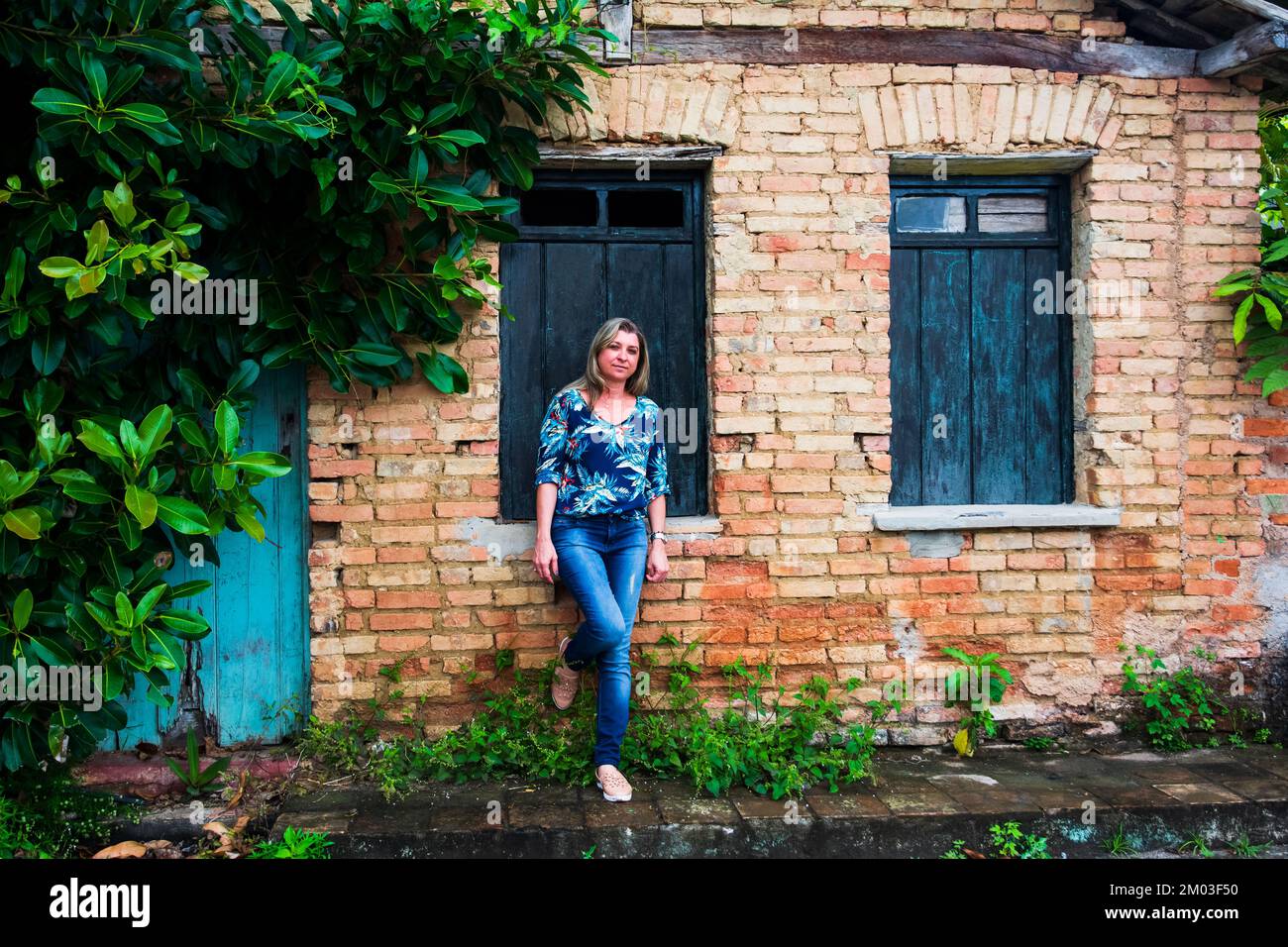 Woman leaning against a window of an old house. Brick facade and leaves ...