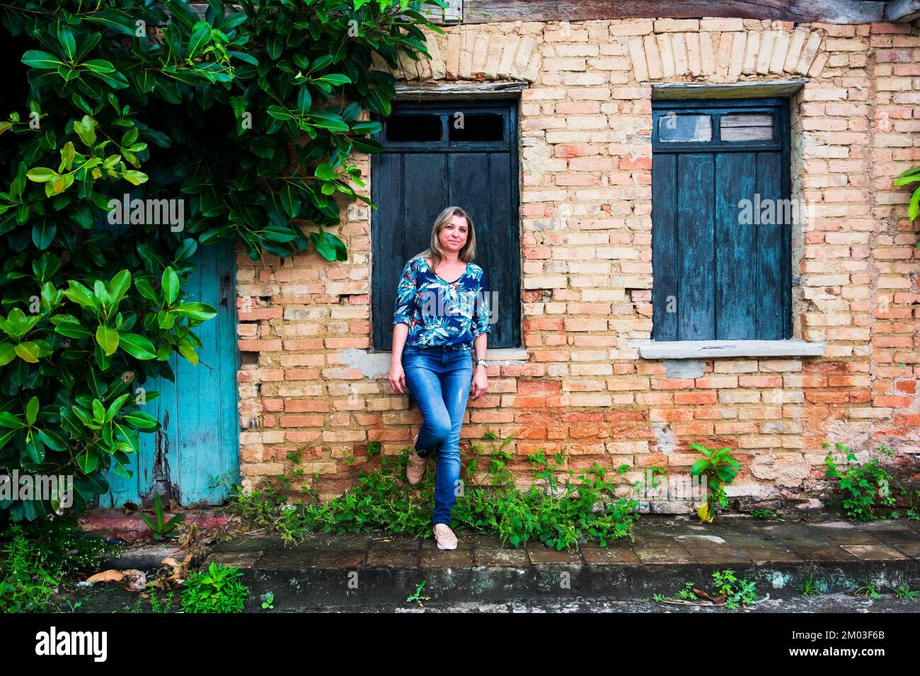 Woman leaning against a window of an old house. Brick facade and leaves ...