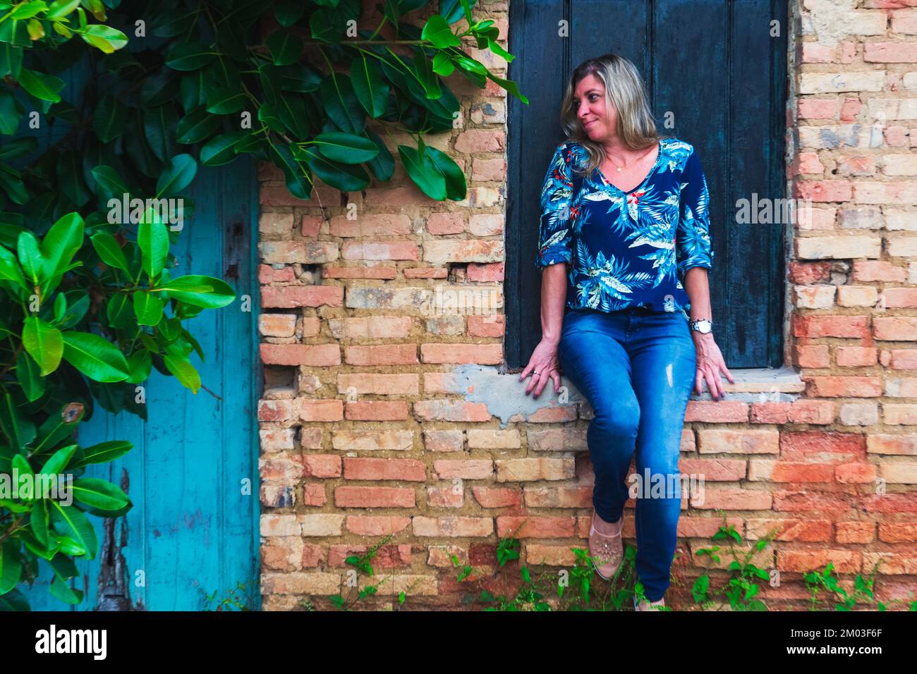 Woman leaning against a window of an old house. Brick facade and leaves ...