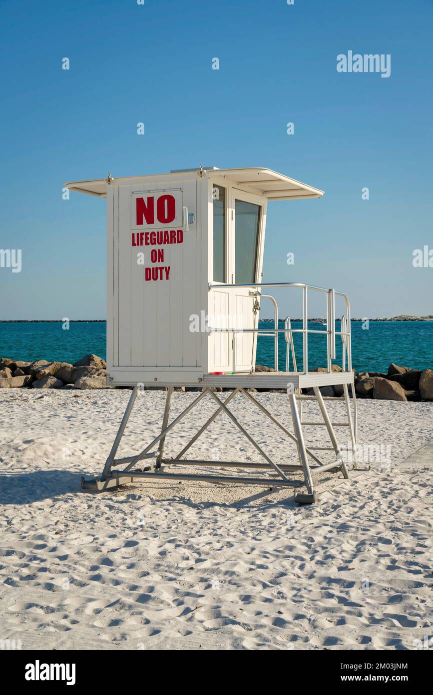 Small white lifeguard tower on a beach shore with rocks near the water ...