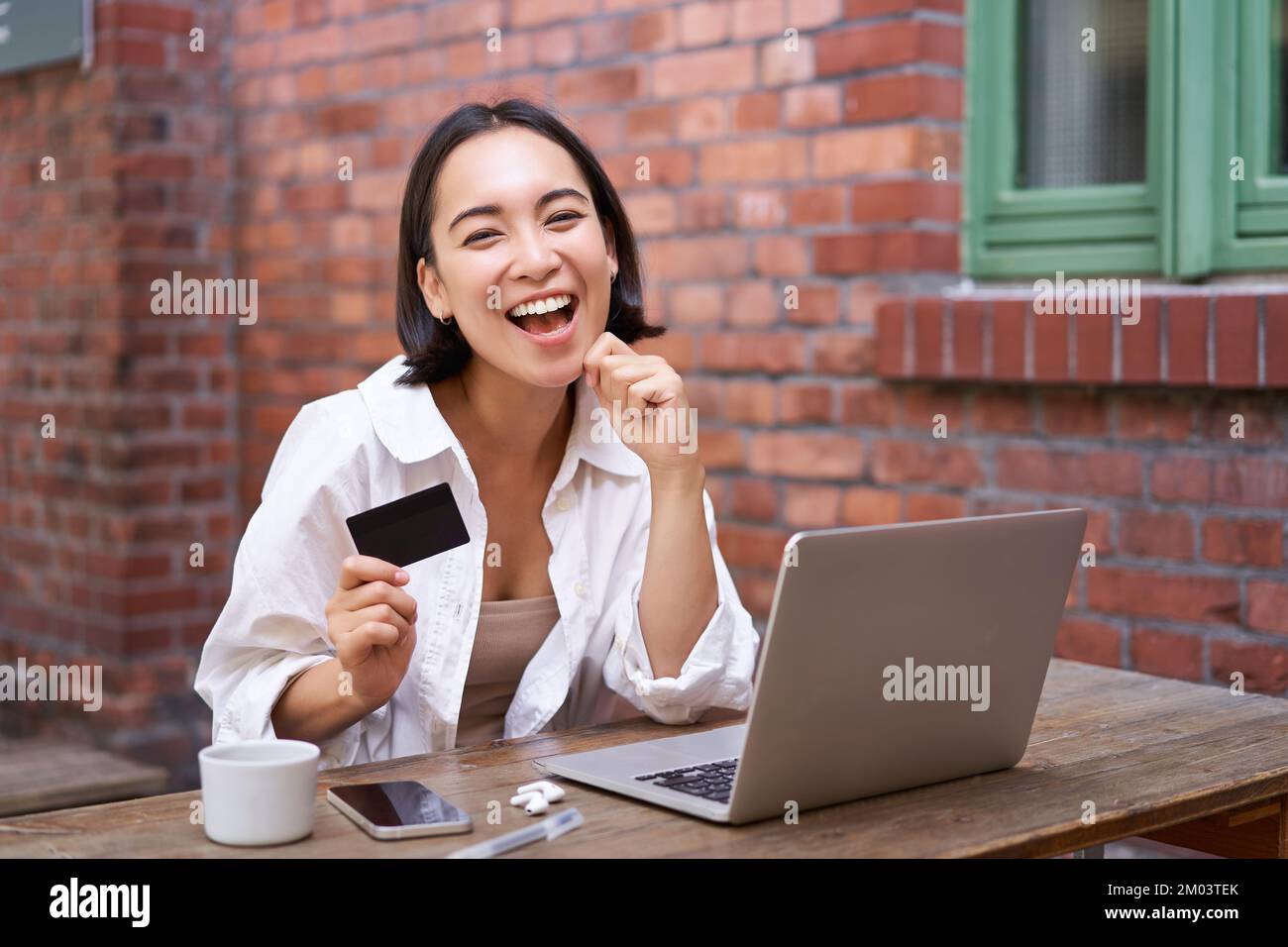 Happy young asian woman sitting near laptop, holding credit card ...