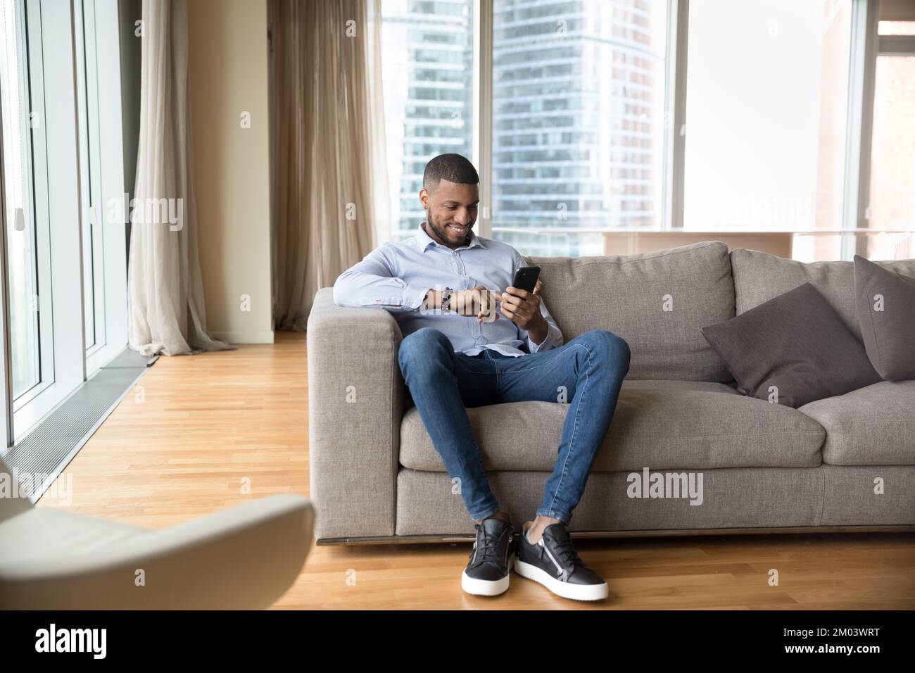 Cheerful African mobile phone user man resting on sofa Stock Photo - Alamy