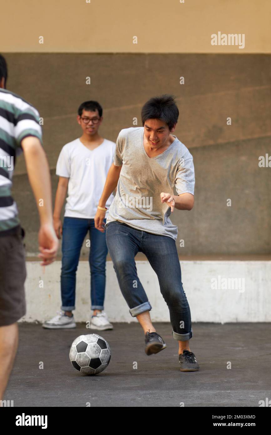 Showing off his mad skills. Three asian teenagers playing soccer in the ...