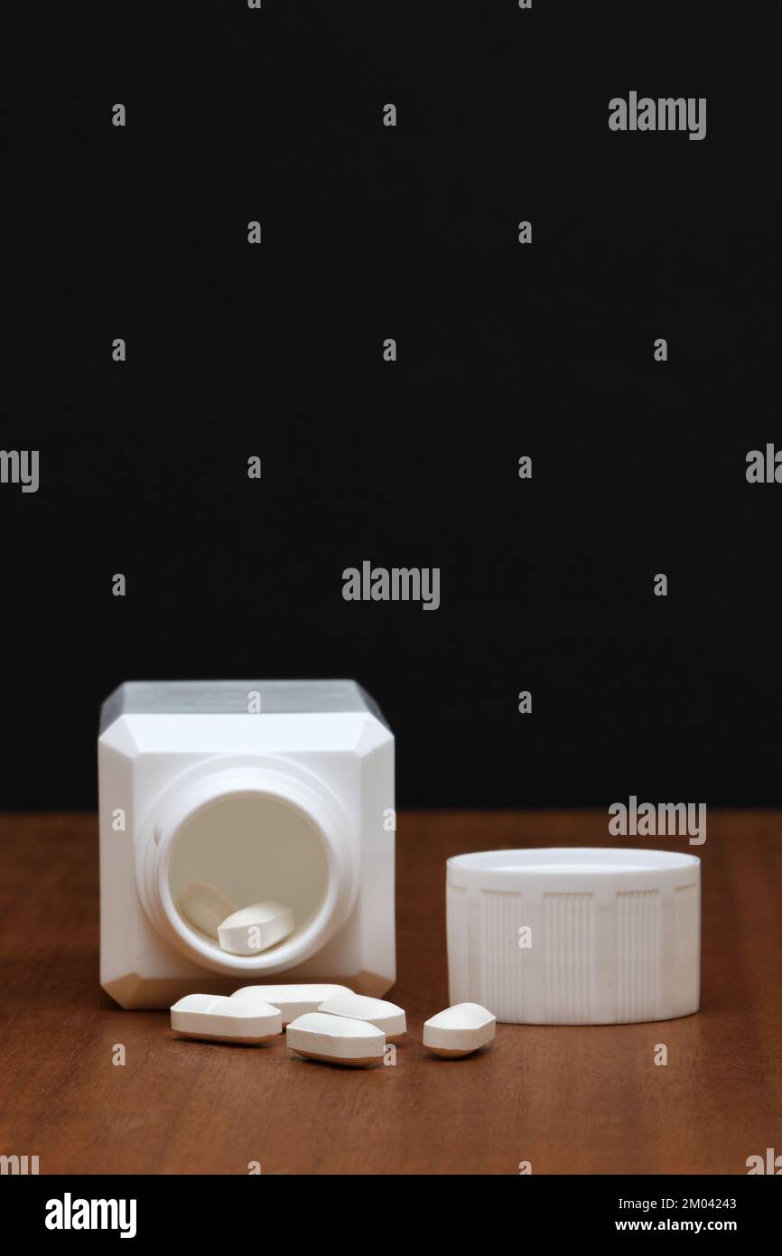 A white, open prescription medication container with some tablets out ...