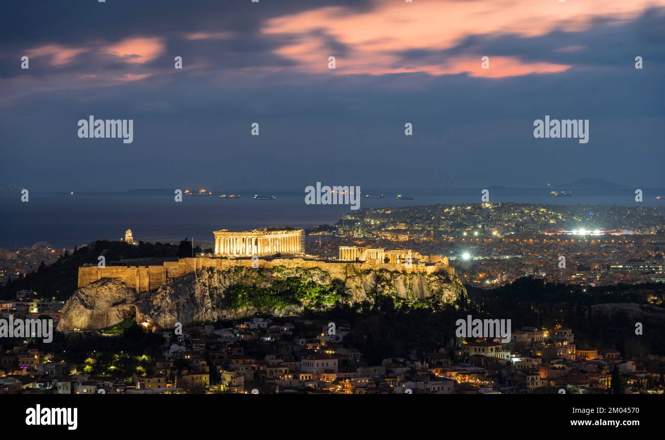 View over the sea of houses of Athens, illuminated Parthenon temple on the Acropolis, dramatic ...