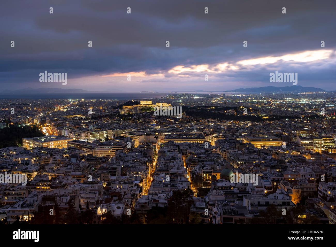 View over the sea of houses of Athens, illuminated Parthenon temple on the Acropolis, dramatic ...