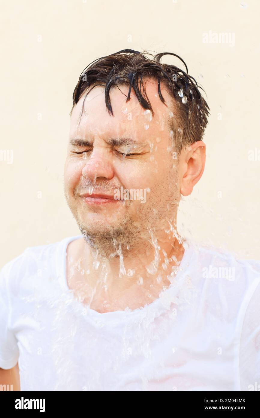 Wet young european white man in white t-shirt with closed eyes in water ...