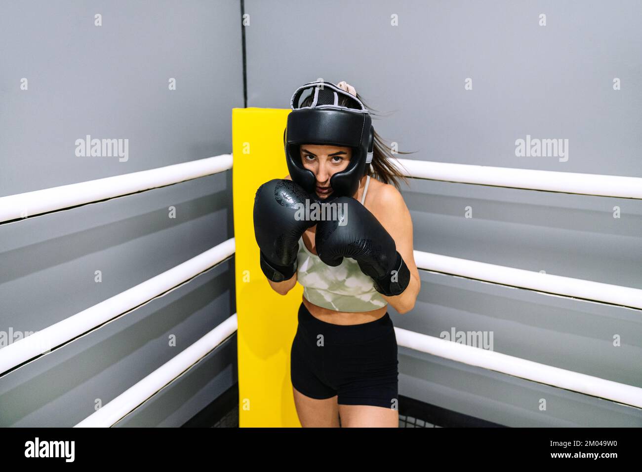 A young woman wearing protective boxing gloves and helmet in fighting ...