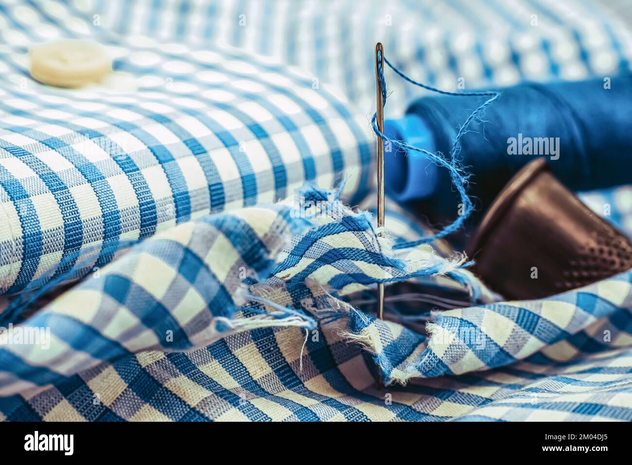 Needle and thread on a checkered fabric close-up. Seamstress or tailor ...
