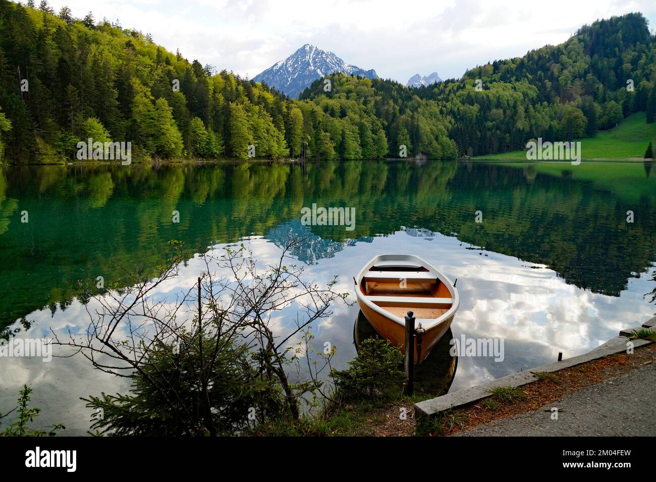 boat resting on emerald-green waters of lake Alatsee in Fuessen ...