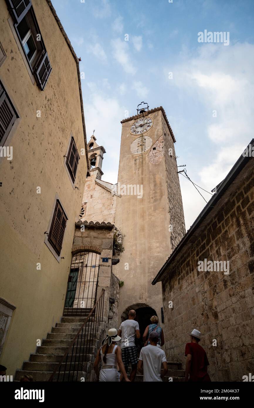 Omis, Croatia-August 18th, 2022: Tourists climbing stone stairs underneath church bell tower at ...