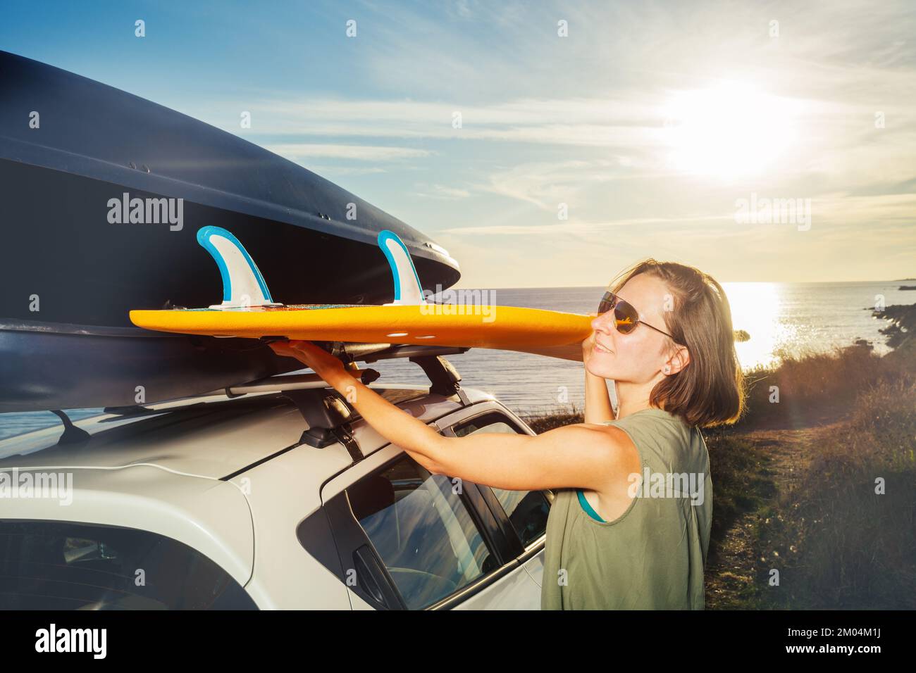 Surfer woman take surfboard from roof top rack baggage on a car Stock ...