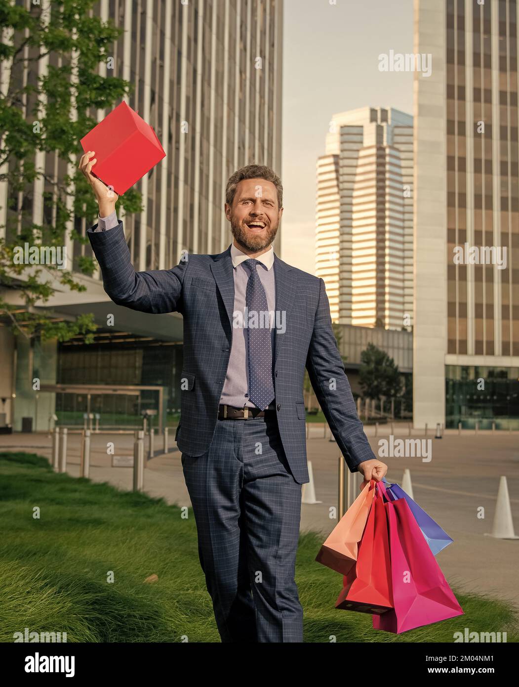 laughing man in formalwear with shopping bags and present box walk ...