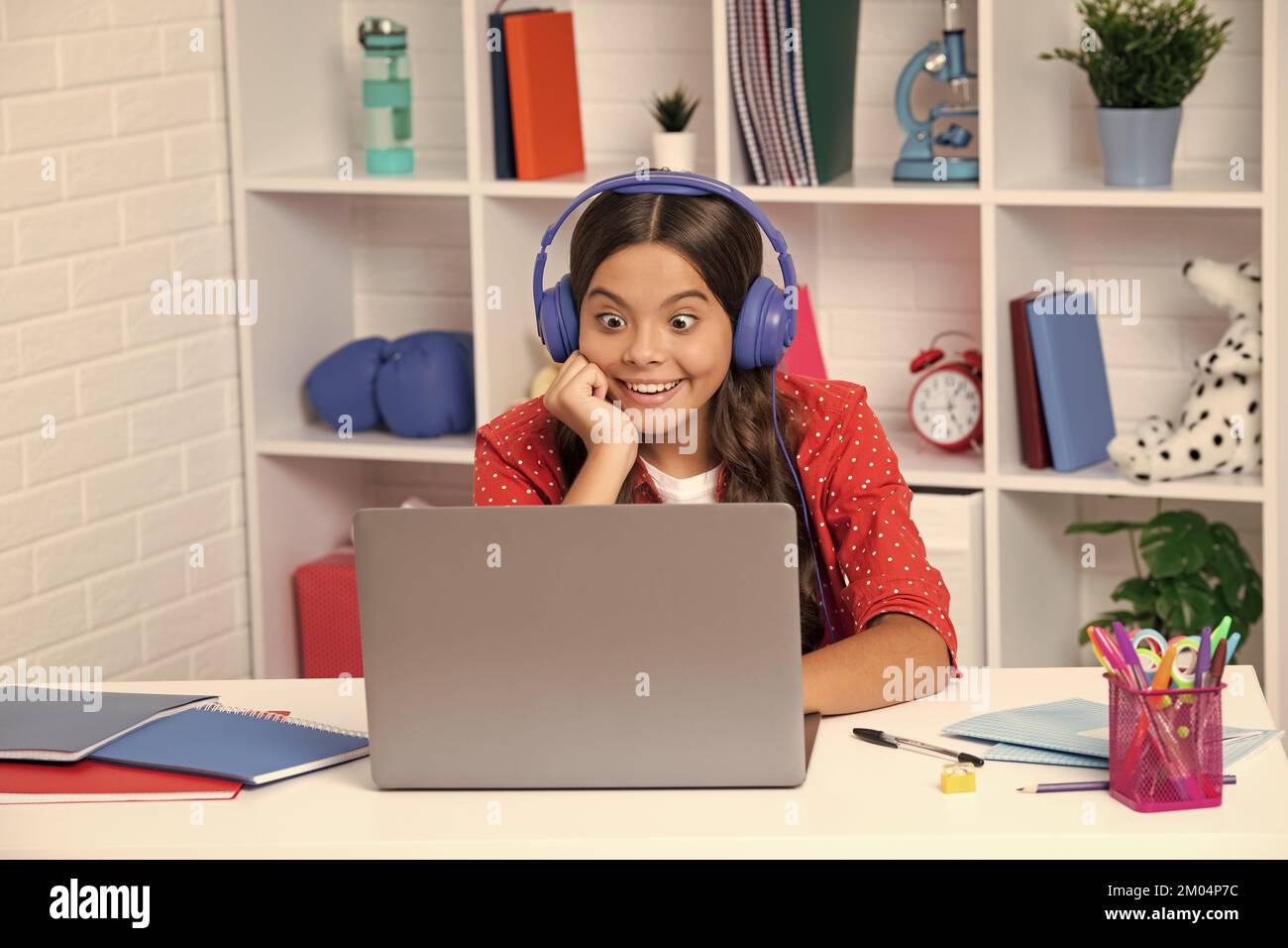 A young female student sitting at the table, using headphones and ...