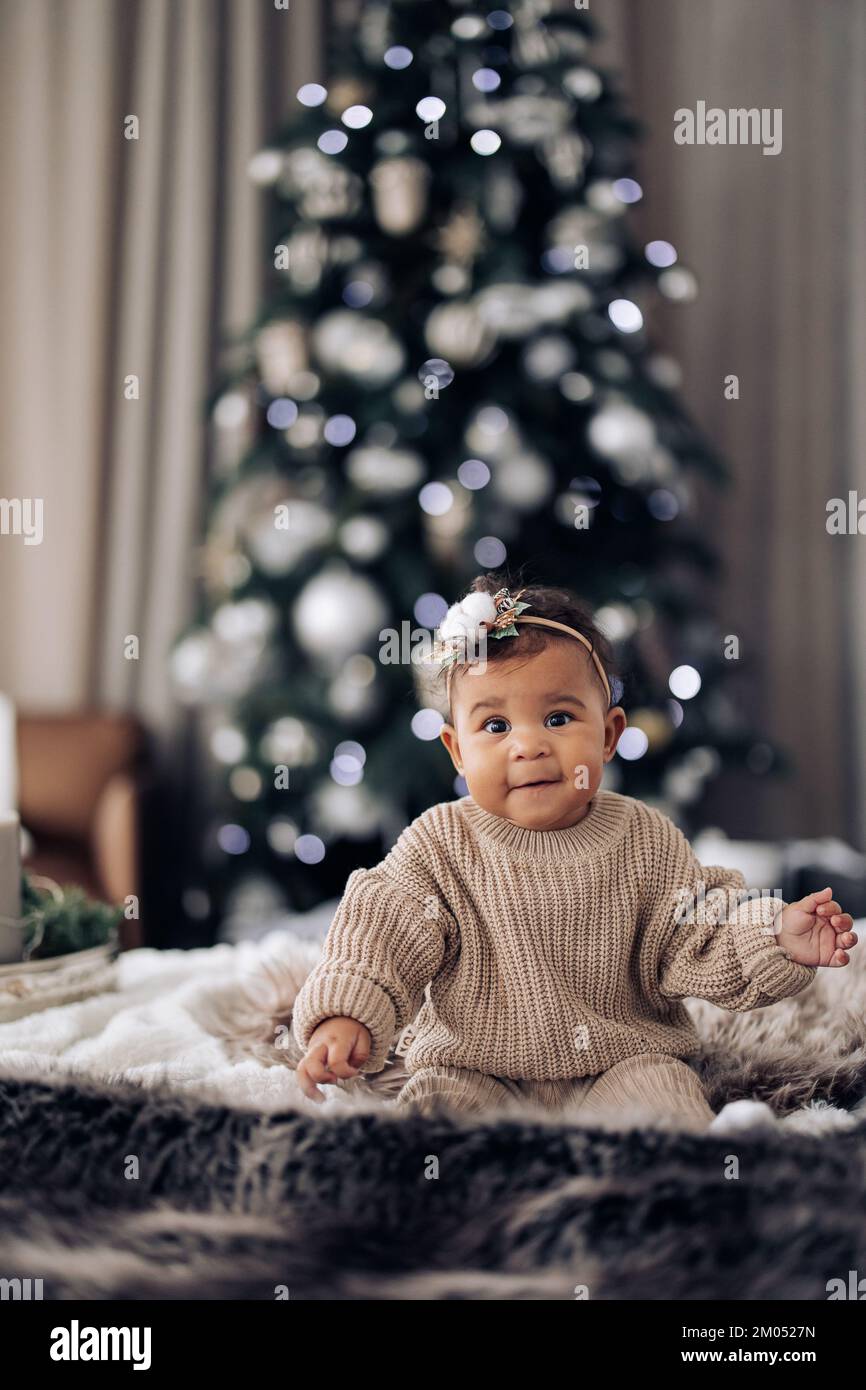 Happy mixed race baby girl sits on bed against background of Christmas ...