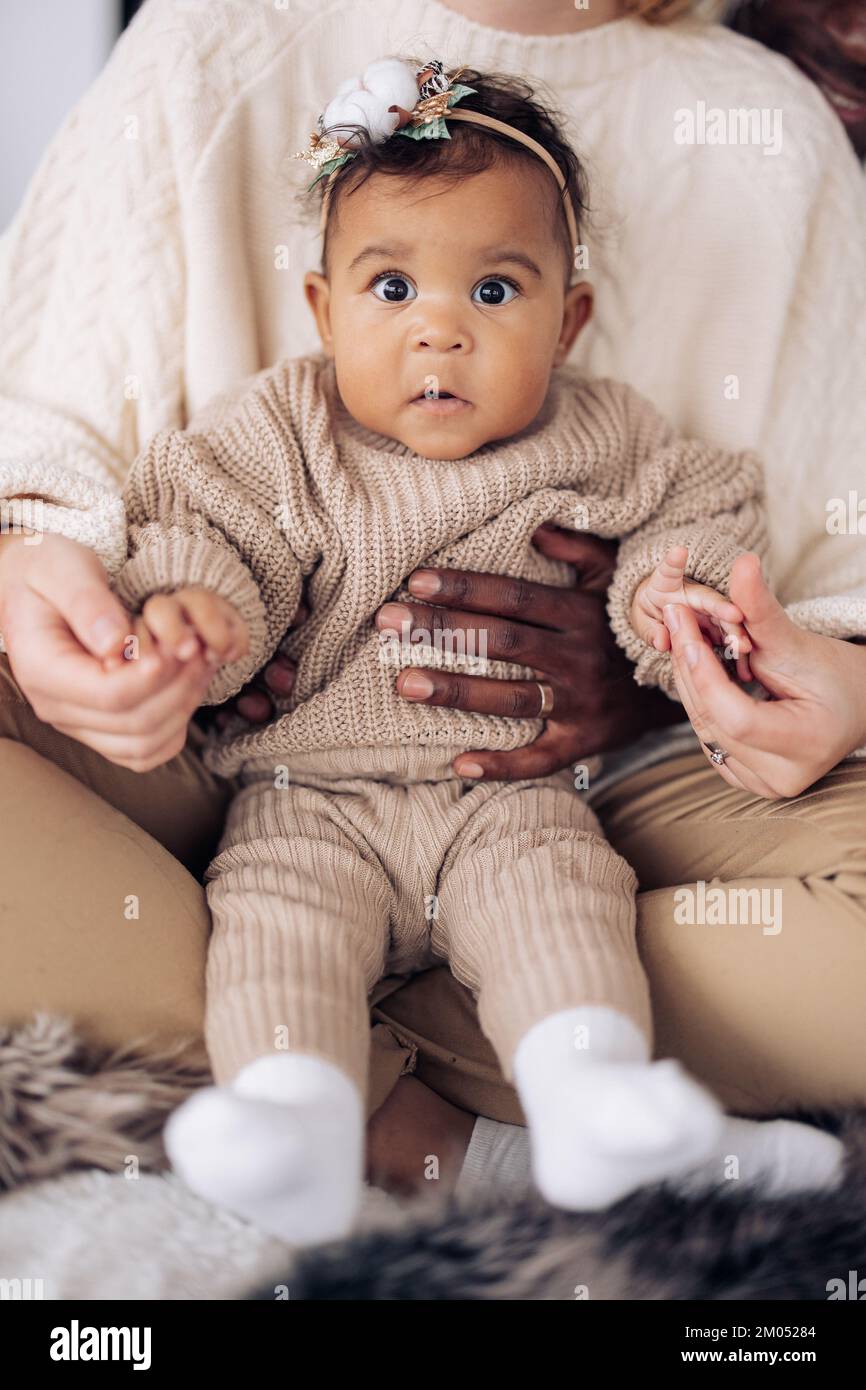 Mixed race baby girl sits near her parents. Hands of parents hold baby ...
