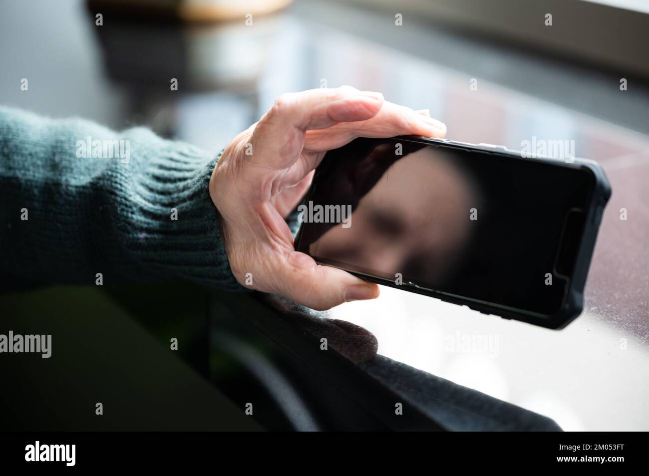 Hand of an 84 yo woman, holding a smartphone, with her face mirrored in ...