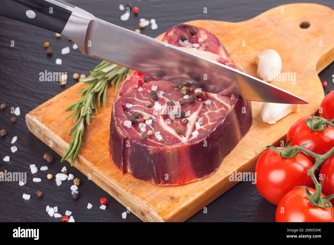 Kitchen knife cuts raw meat beef steak with bone, spices, rosemary and ...