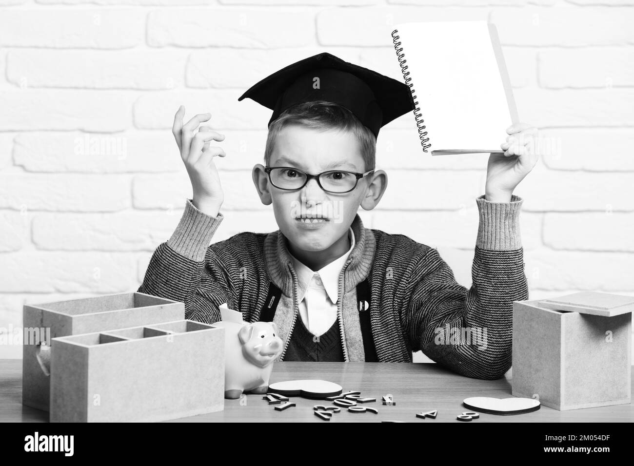 young cute pupil boy in grey sweater and glasses sitting at desk with ...