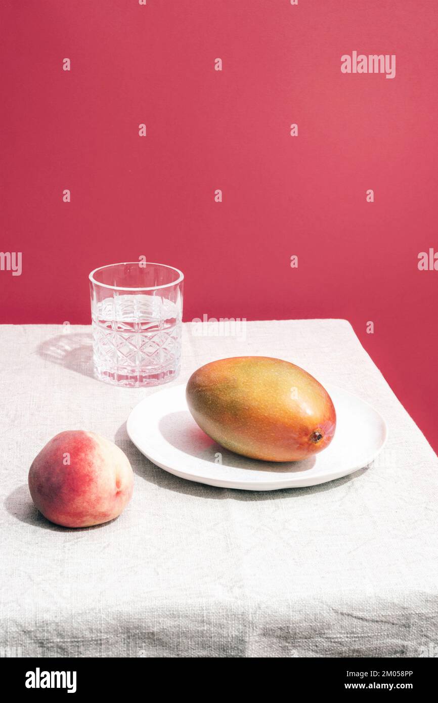 Ripe mango on a plate, peach fruit and a glass of water on a table ...
