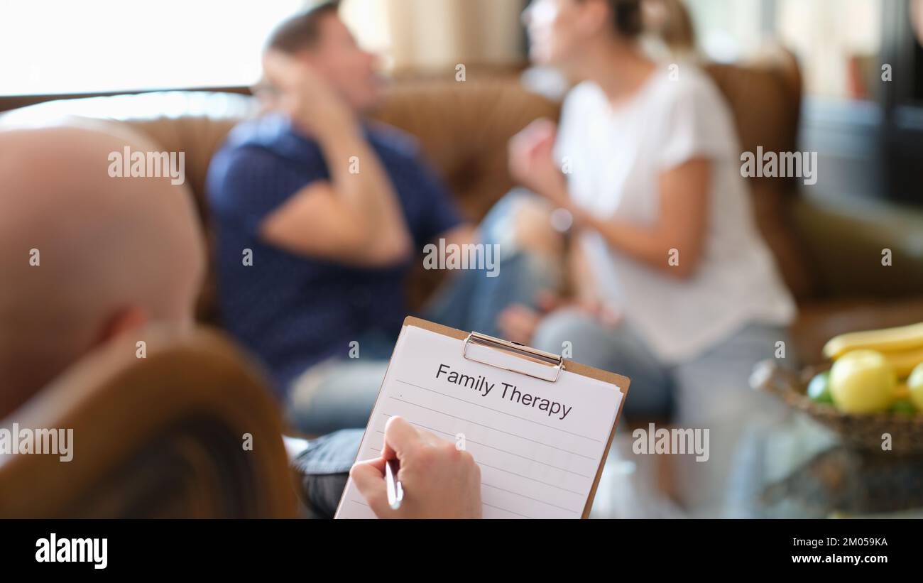 Family therapist takes notes on his paper while listening to couples ...