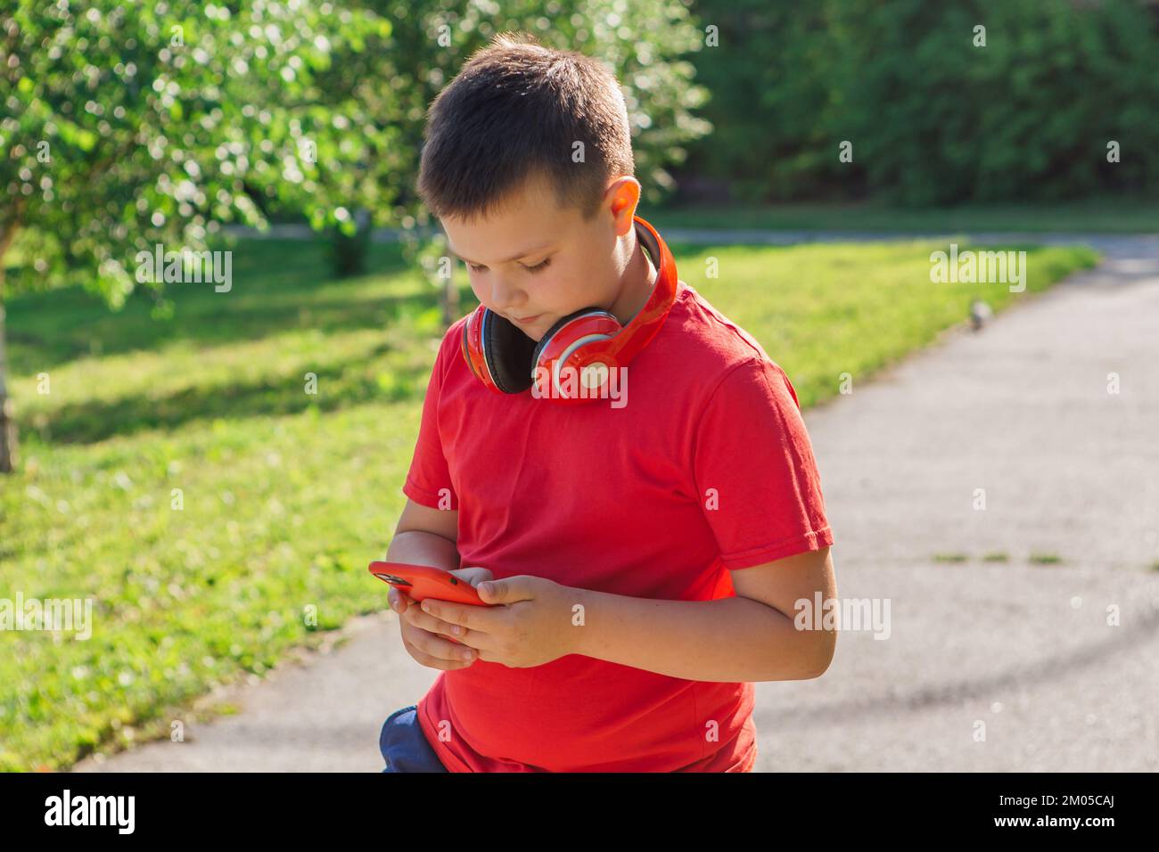 Happy chubby ten years old boy with headphones outdoors. Boy chating on ...