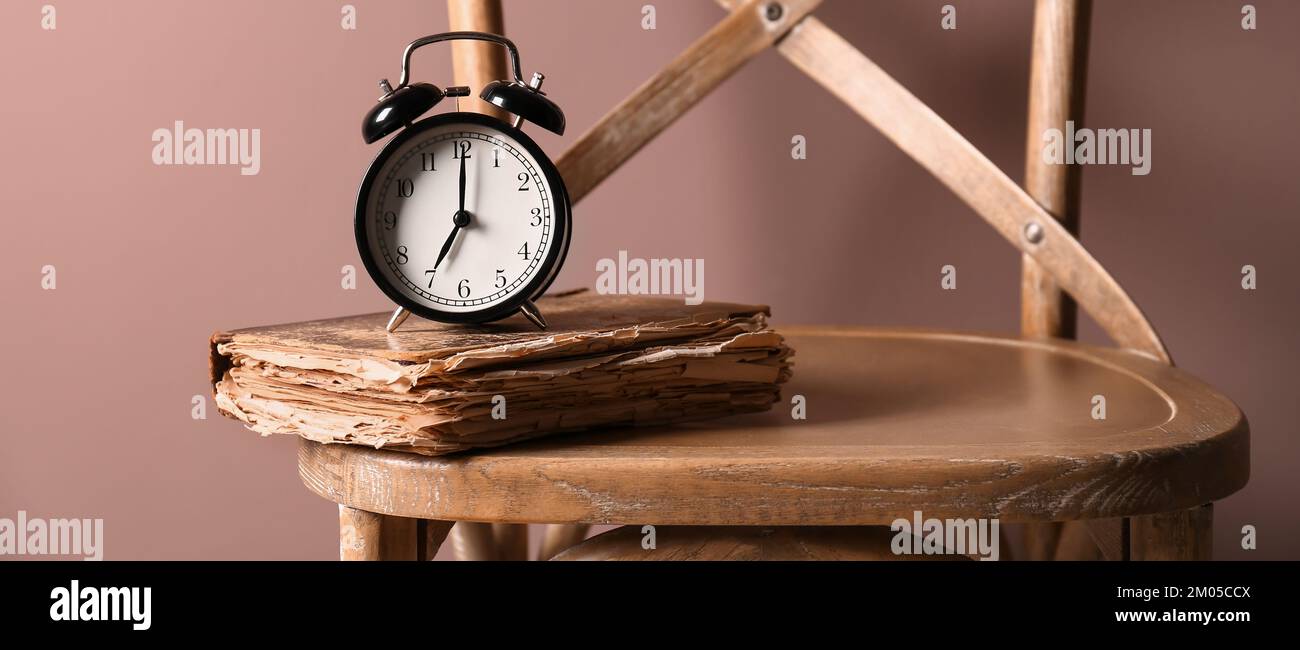 Alarm clock and old book on chair against beige background Stock Photo ...