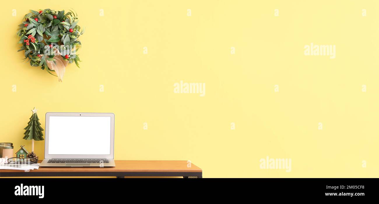 Laptop with Christmas decor at workplace near yellow wall with space ...