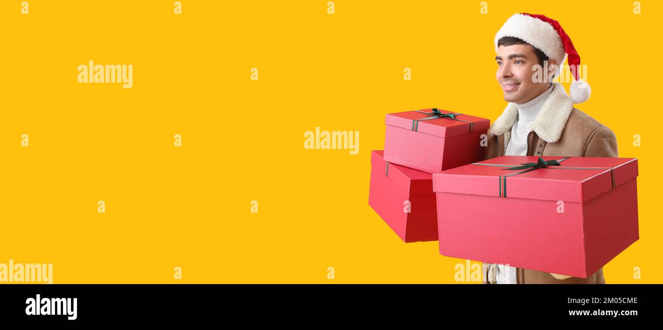 Happy young man in Santa hat holding Christmas present on yellow ...