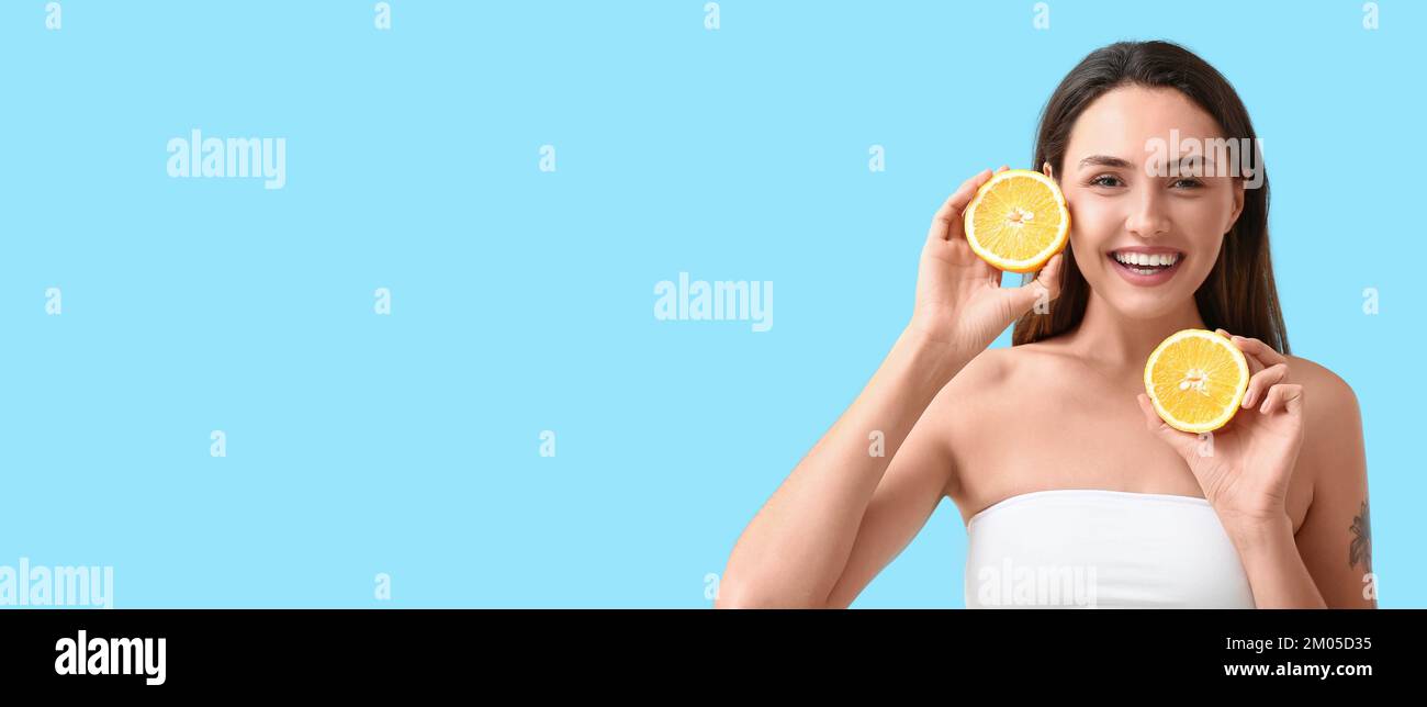 Beautiful young woman with fresh cut orange on light blue background ...