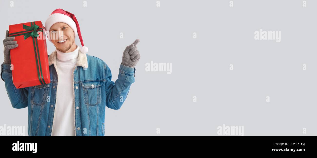 Handsome man in Santa hat holding Christmas present and pointing at ...