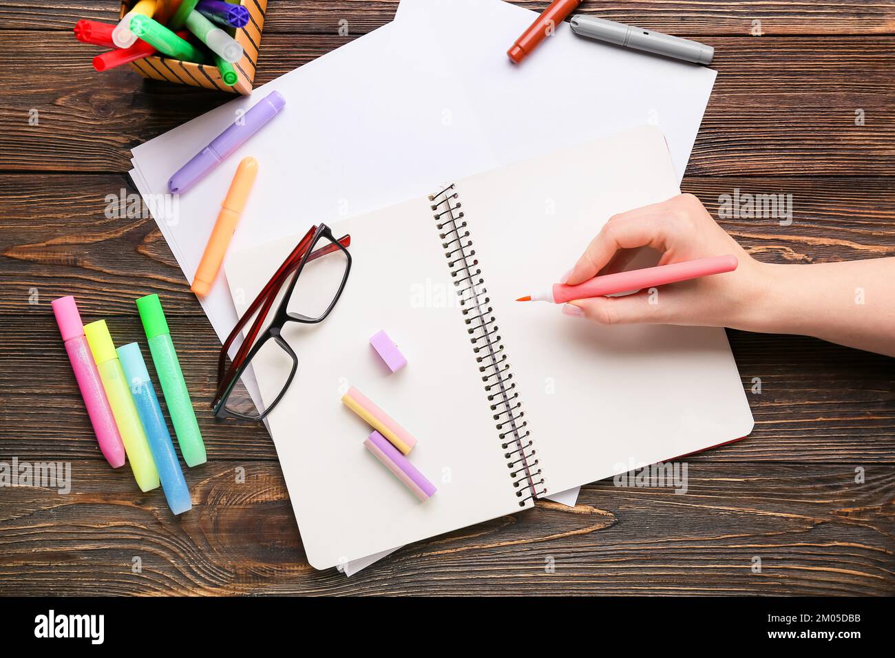 Woman with felt-tip pen, notebook, paper sheets and eyeglasses on dark ...