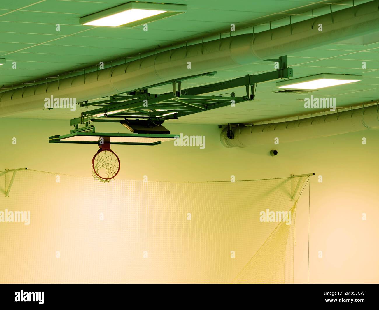 Folded basketball hoop bellow ceiling. The basket with white net in ...