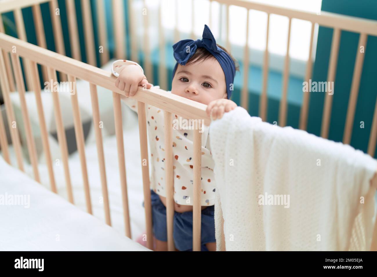 Adorable toddler standing on cradle with relaxed expression at bedroom ...