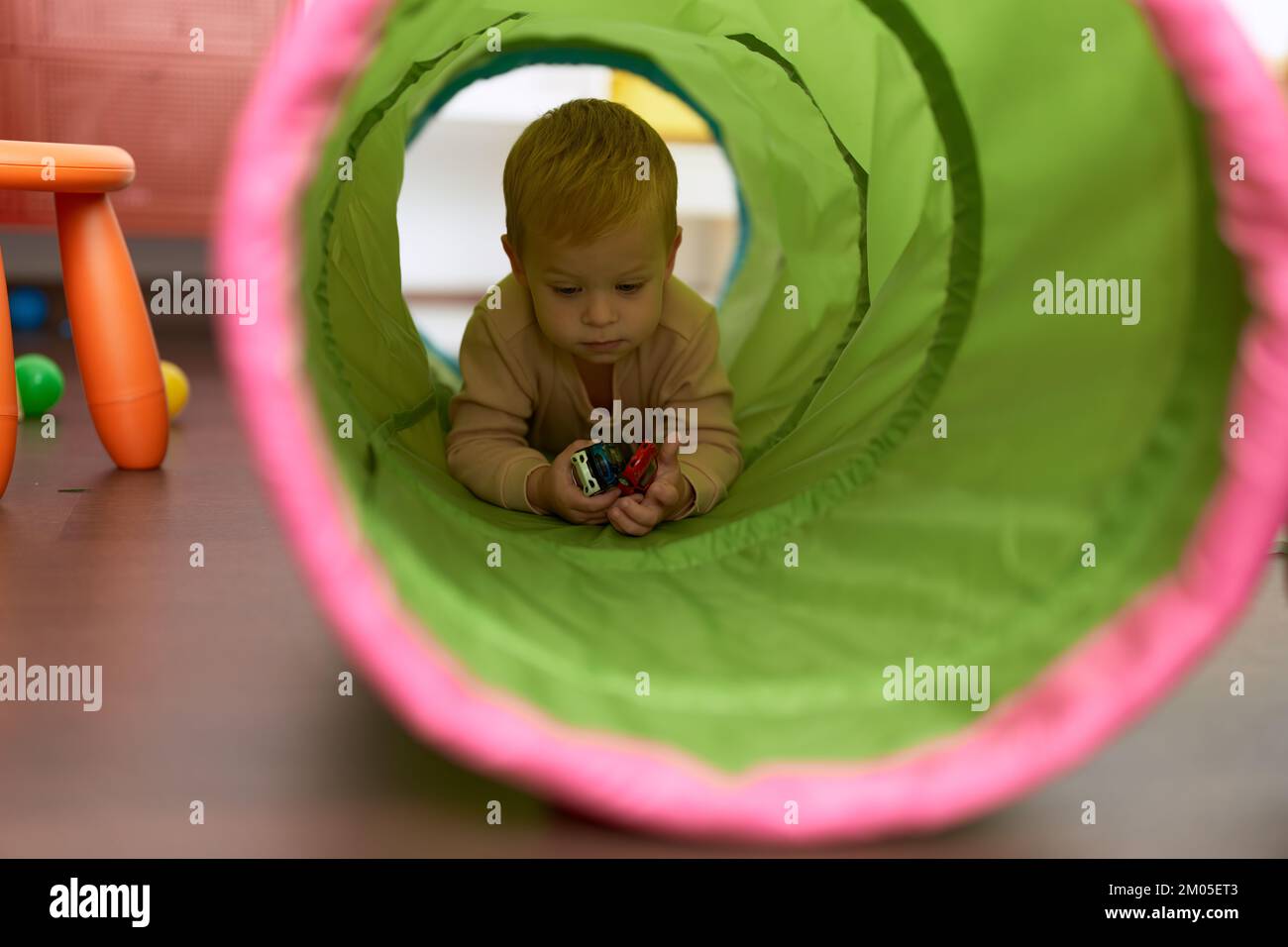 Adorable toddler crawling throw tunnel toy holding cars at kindergarten ...