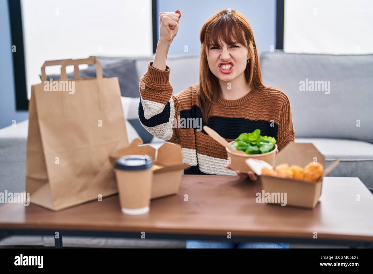 Young beautiful woman eating delivery food at the living room annoyed ...