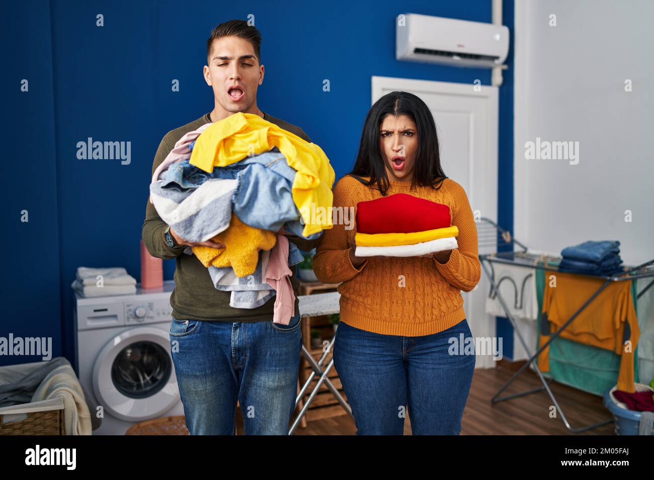 Young couple holding laundry dirty and clean laundry in shock face ...
