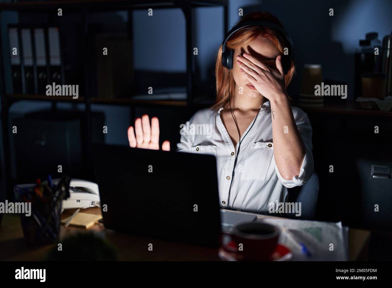 Young caucasian woman working at the office at night covering eyes with ...