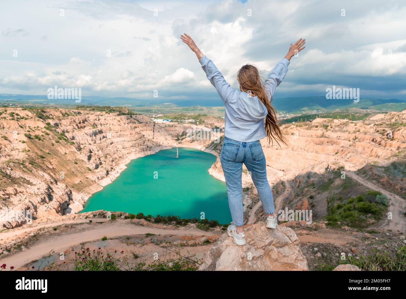 Girl on top of a mountain with raised hands, view of the azure lake in ...