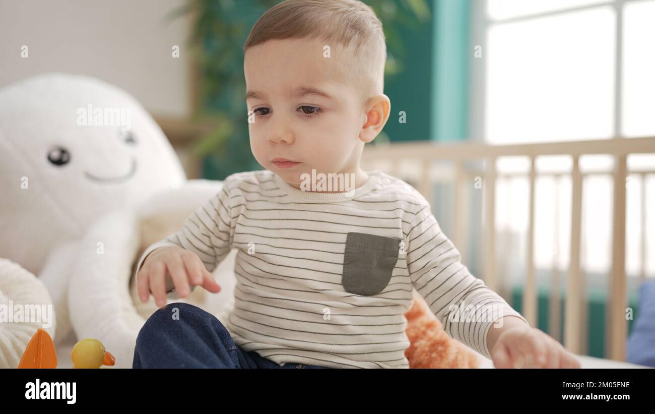 Adorable toddler sitting on bed with serious expression at bedroom ...