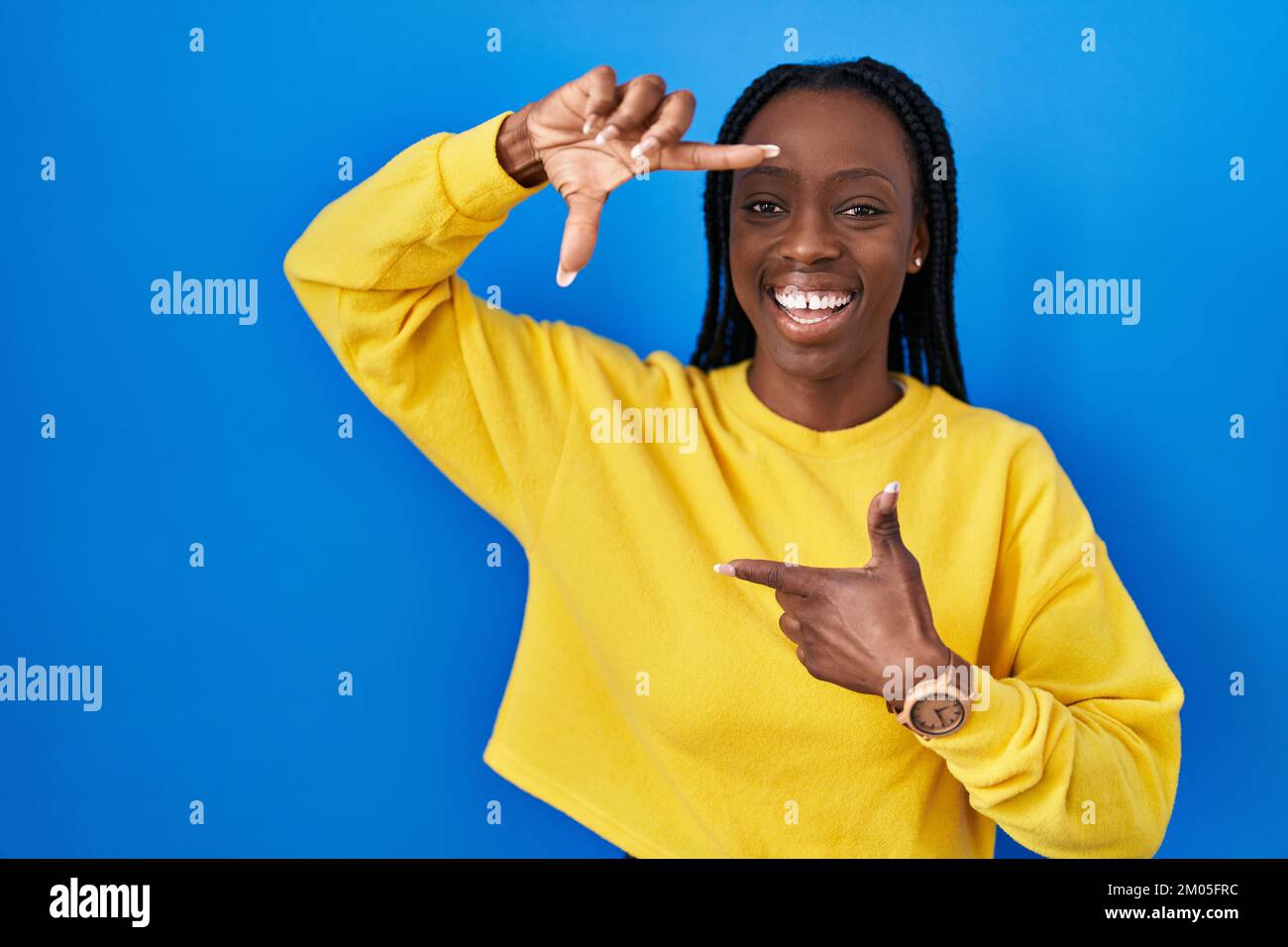 Beautiful black woman standing over blue background smiling making ...