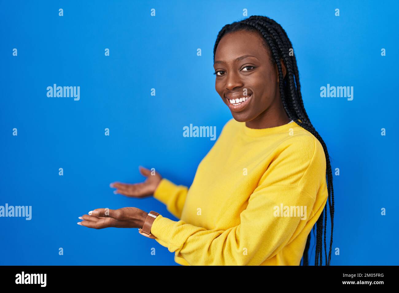 Beautiful black woman standing over blue background inviting to enter ...