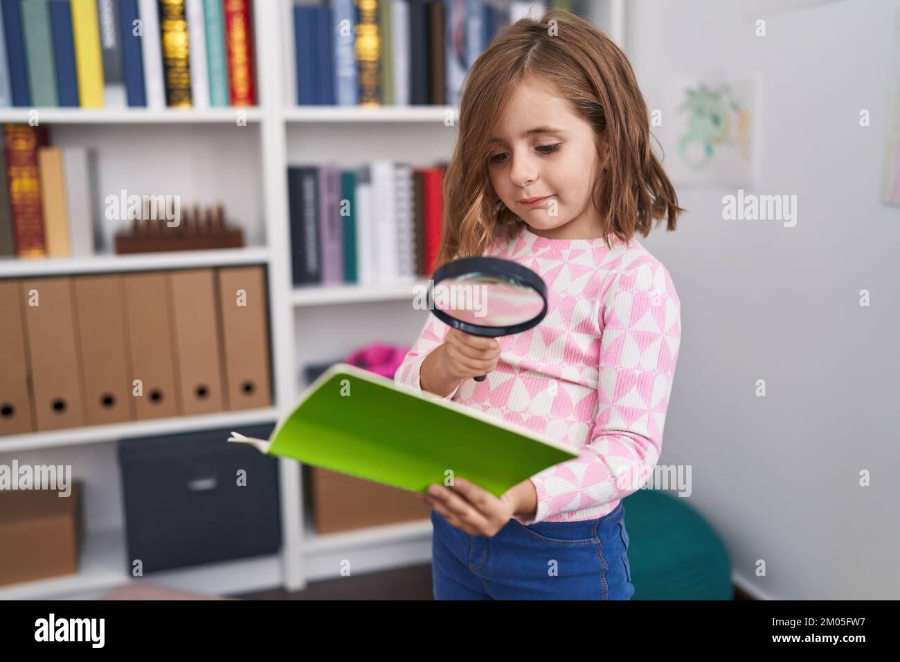 Adorable hispanic girl student reading book using magnifying glass at ...