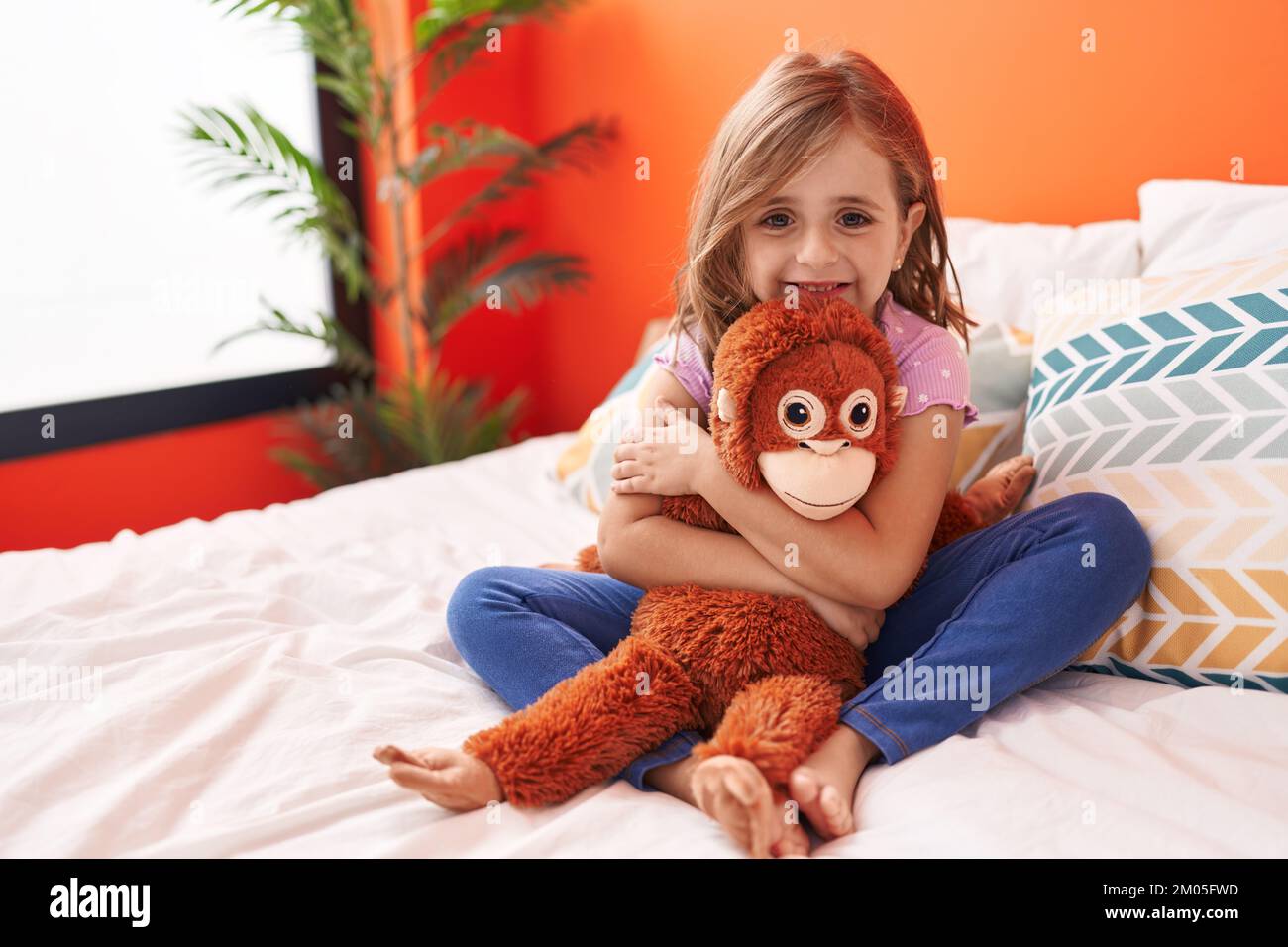 Adorable hispanic girl hugging monkey doll sitting on bed at bedroom ...