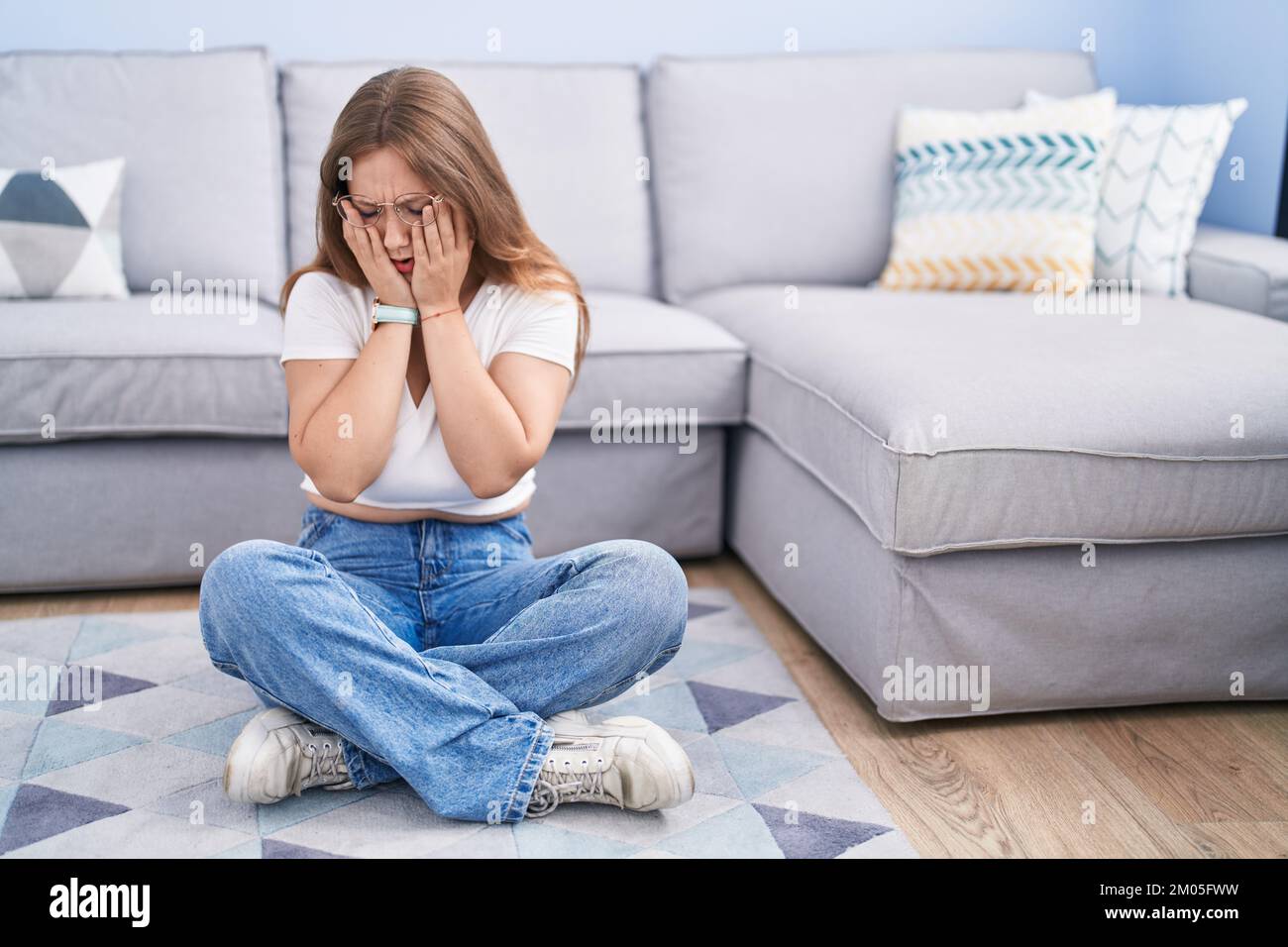 Young caucasian woman sitting on the floor at the living room with sad ...