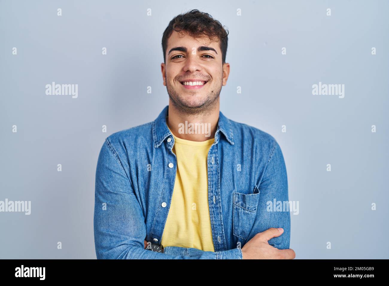 Young hispanic man standing over blue background happy face smiling ...