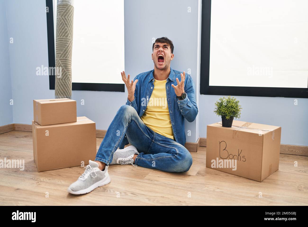 Young hispanic man sitting on the floor at new home crazy and mad ...